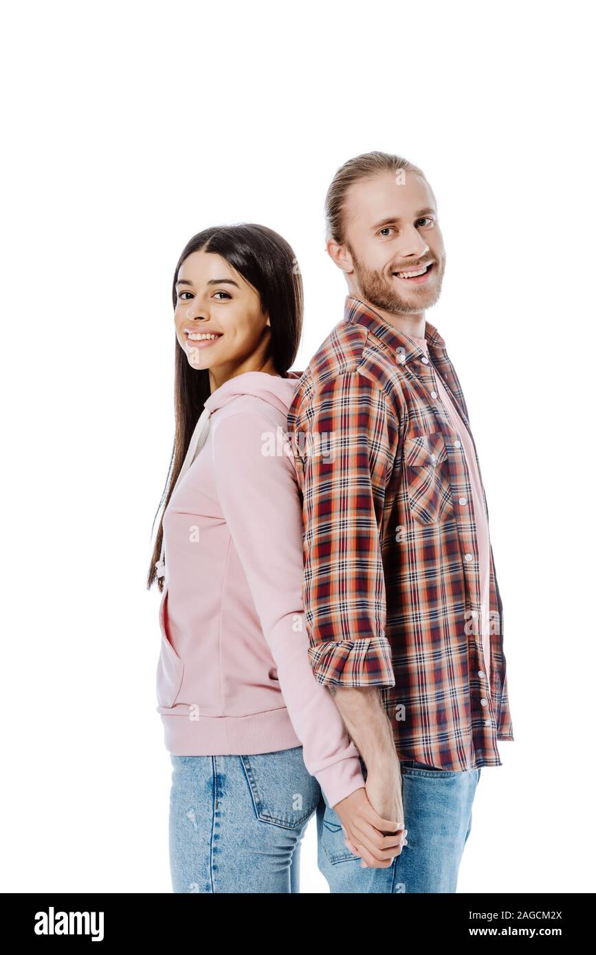 happy young interracial couple standing back to back and holding hands ...