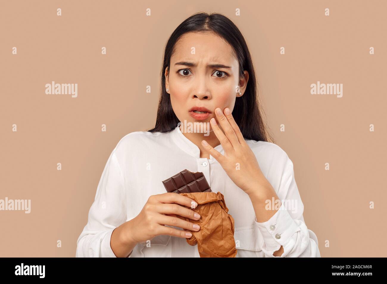 Freestyle. Young woman in shirt standing isolated on bage eating ...