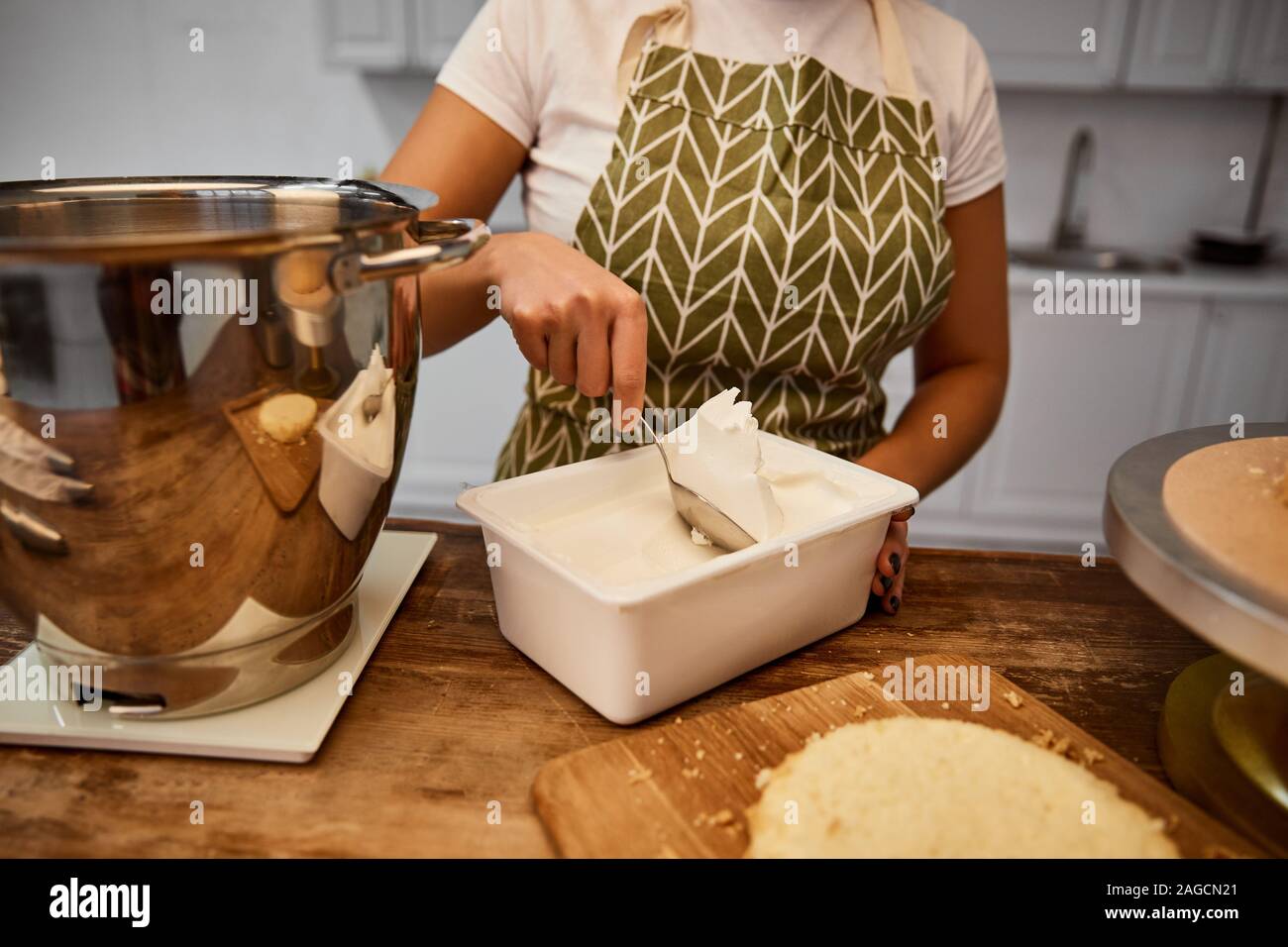 Partial view of confectioner taking cream from container for cooking ...