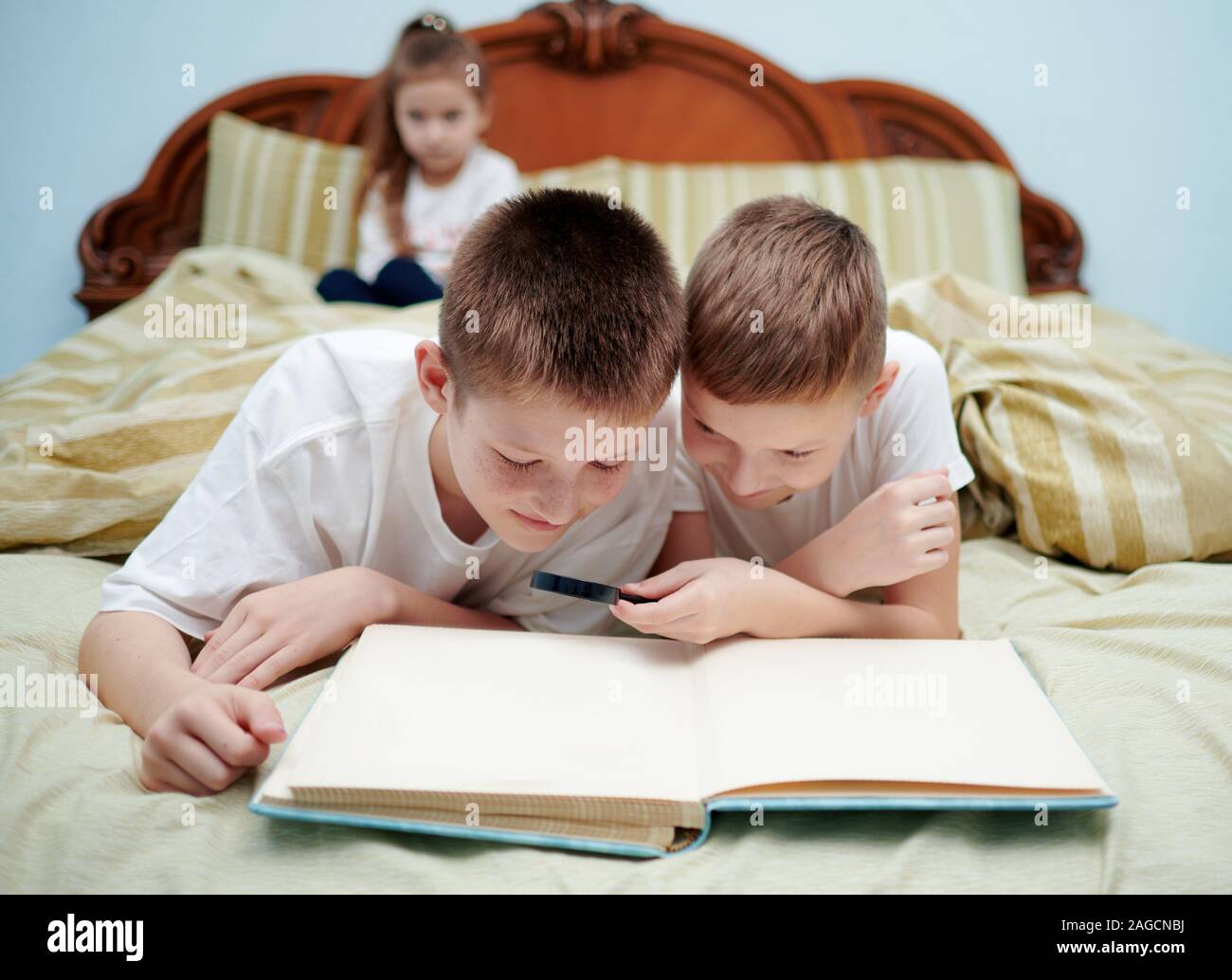 Three children are looking into a book only Stock Photo - Alamy