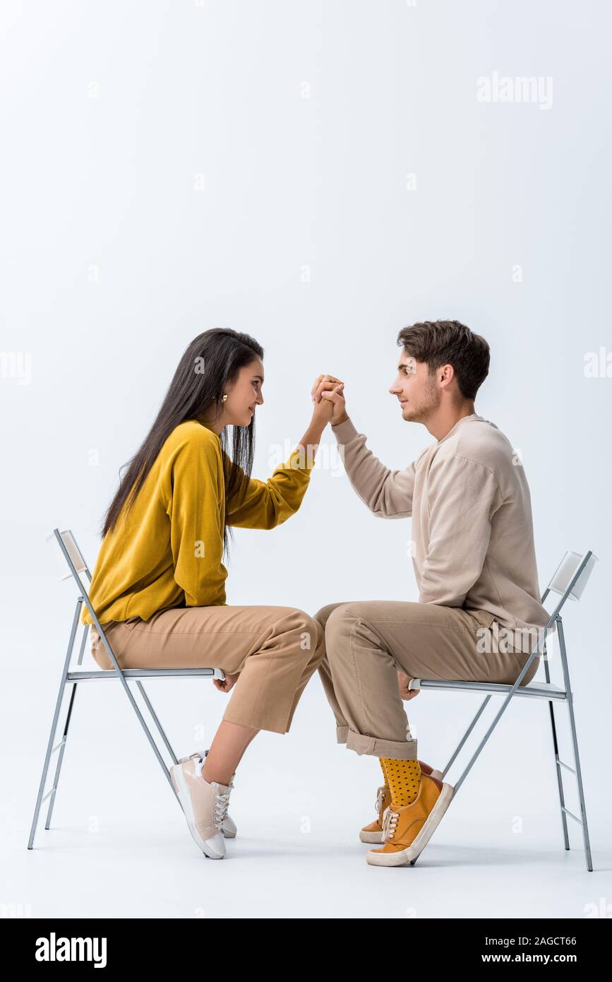 side view of handsome man and woman holding hands while sitting on ... side view of handsome man and woman holding hands while sitting on ...