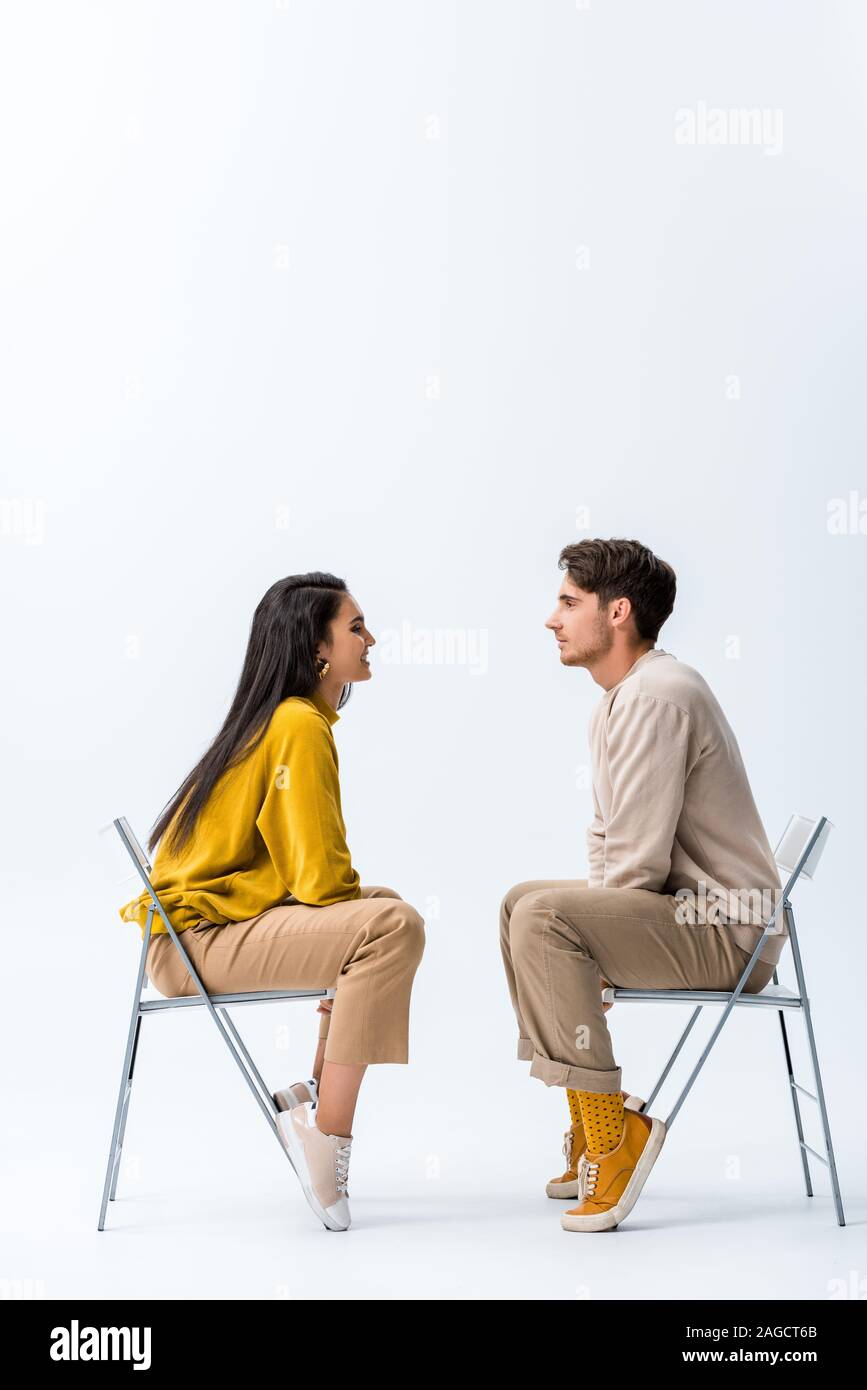 side view of handsome man sitting on chair near cheerful woman on white ...