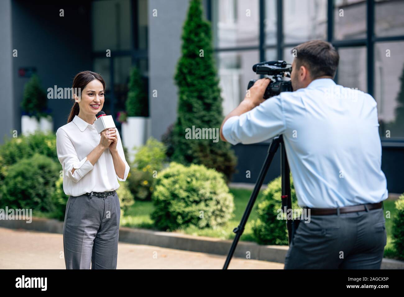 attractive journalist holding microphone and cameraman shooting her ...