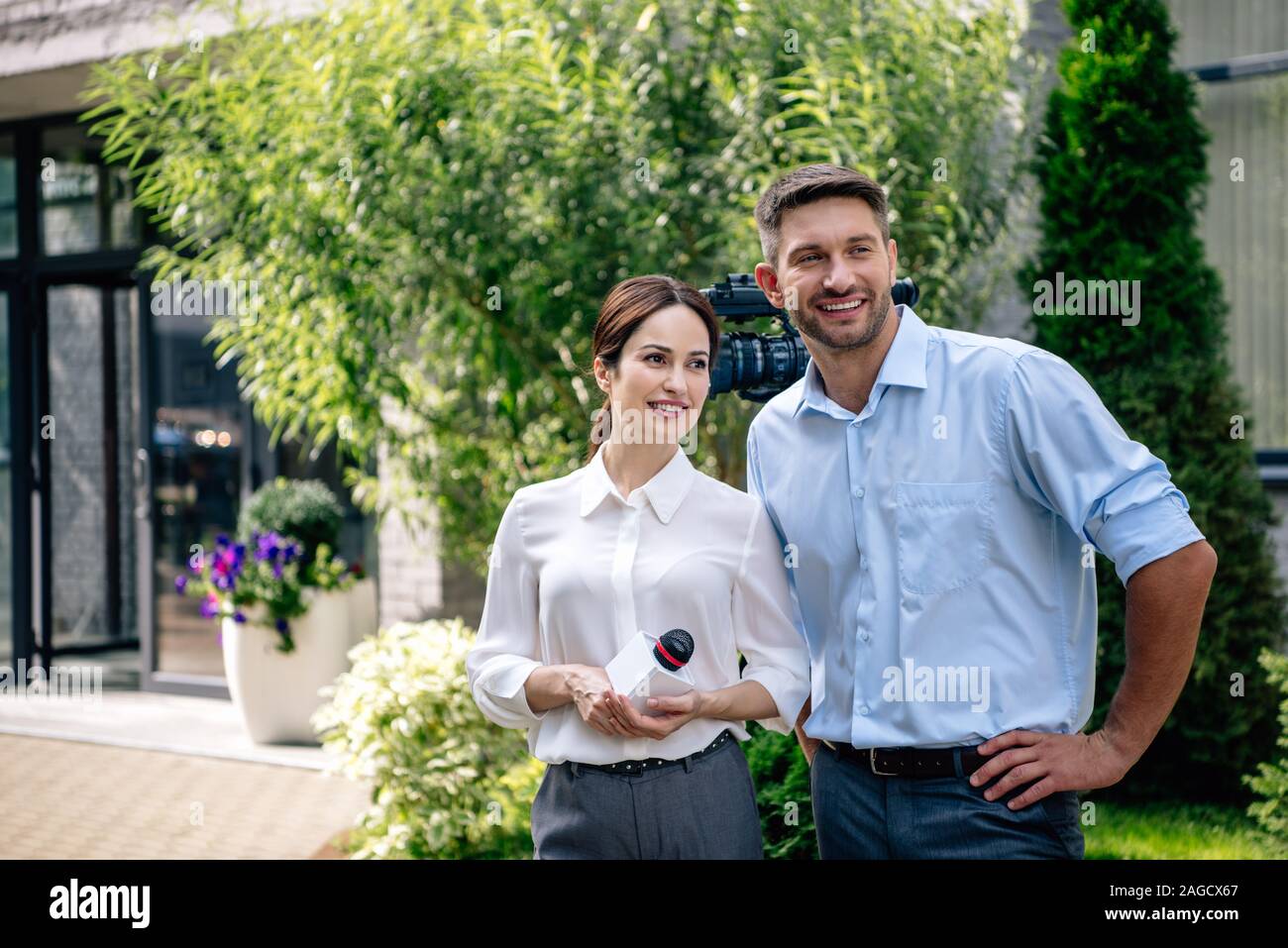 attractive journalist holding microphone and cameraman smiling and ...