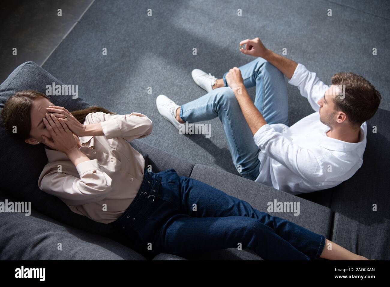 overhead view of crying upset woman on sofa and man sitting on floor in ...