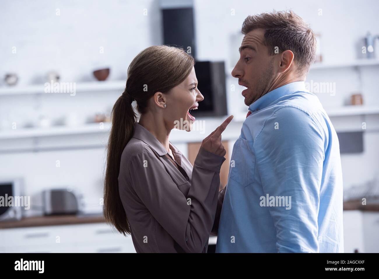 side view of angry woman pointing with finger and screaming at husband ...