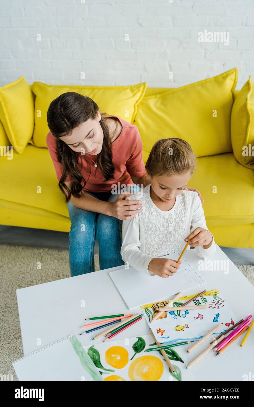 beautiful babysitter sitting on yellow sofa near kid looking at drawn ...