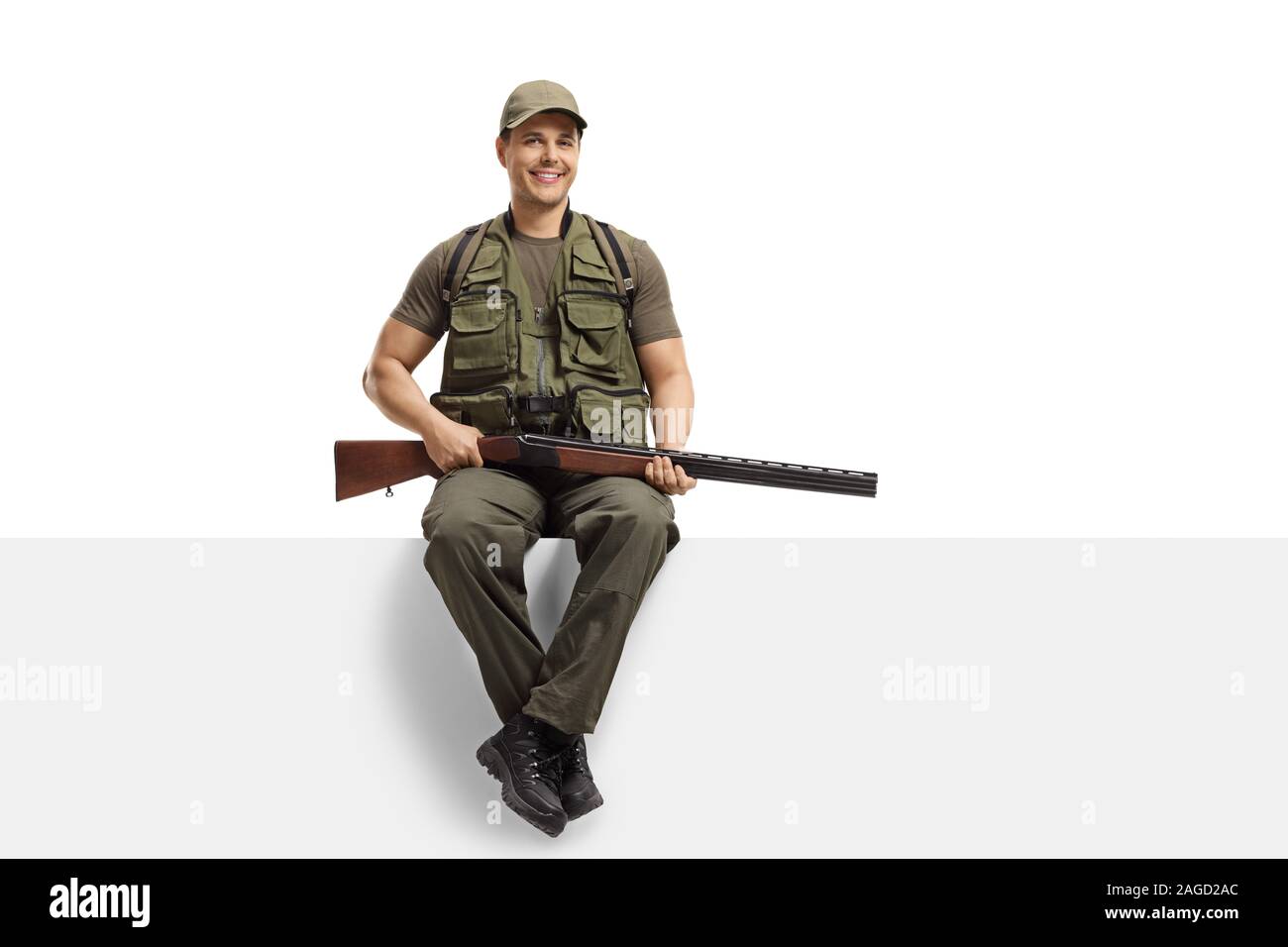 Young man hunter with a rifle sitting on a blank board isolated on ...