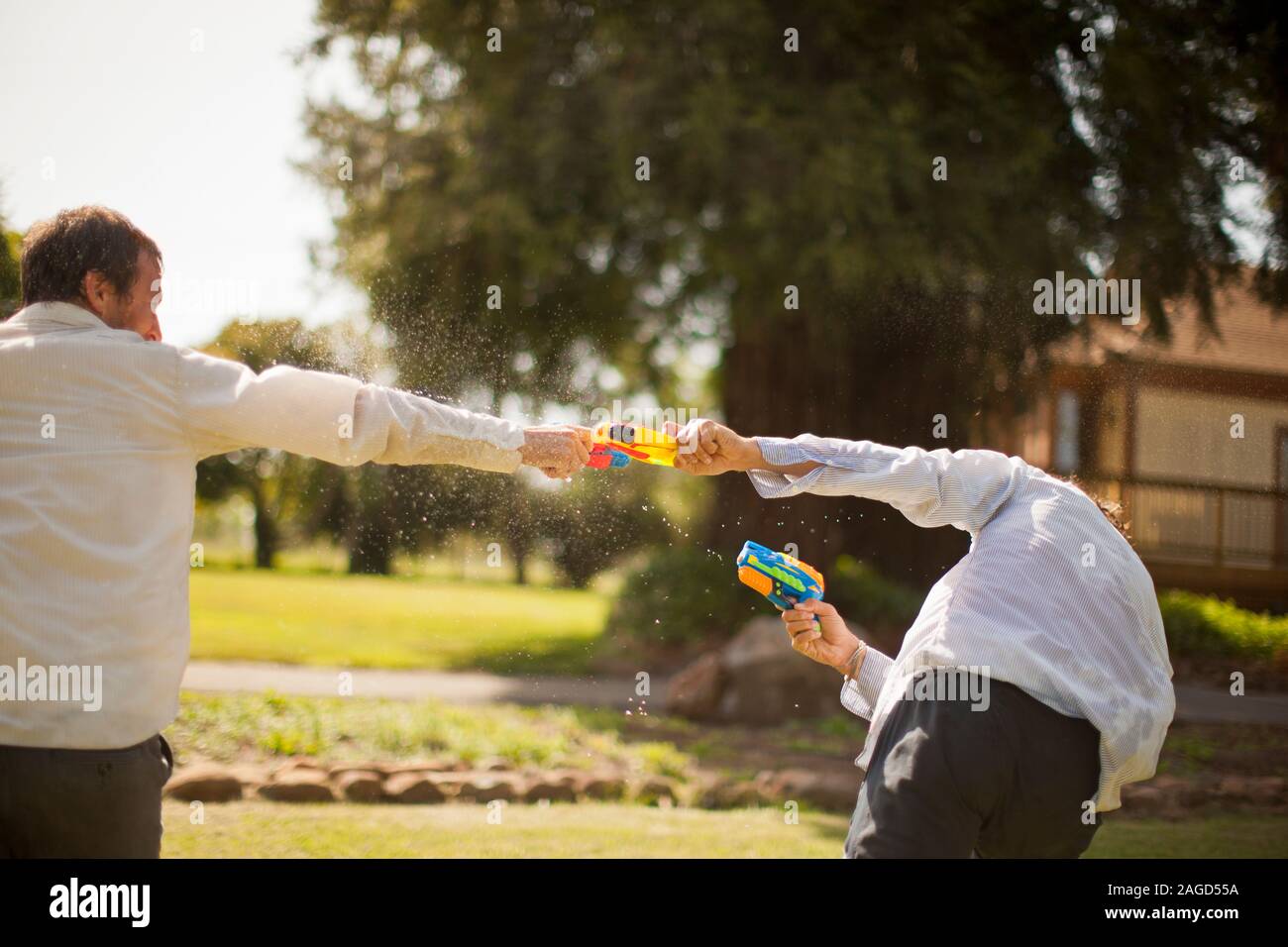 Two men having a water gun fight in a backyard Stock Photo - Alamy