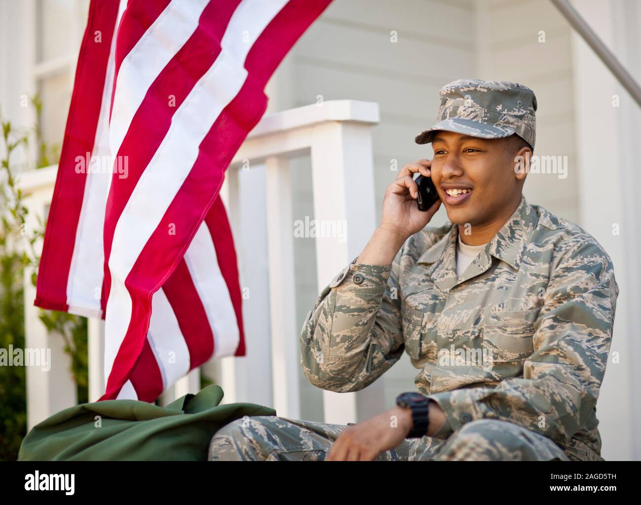 Young adult soldier talking on a cell phone on the porch of his home ...