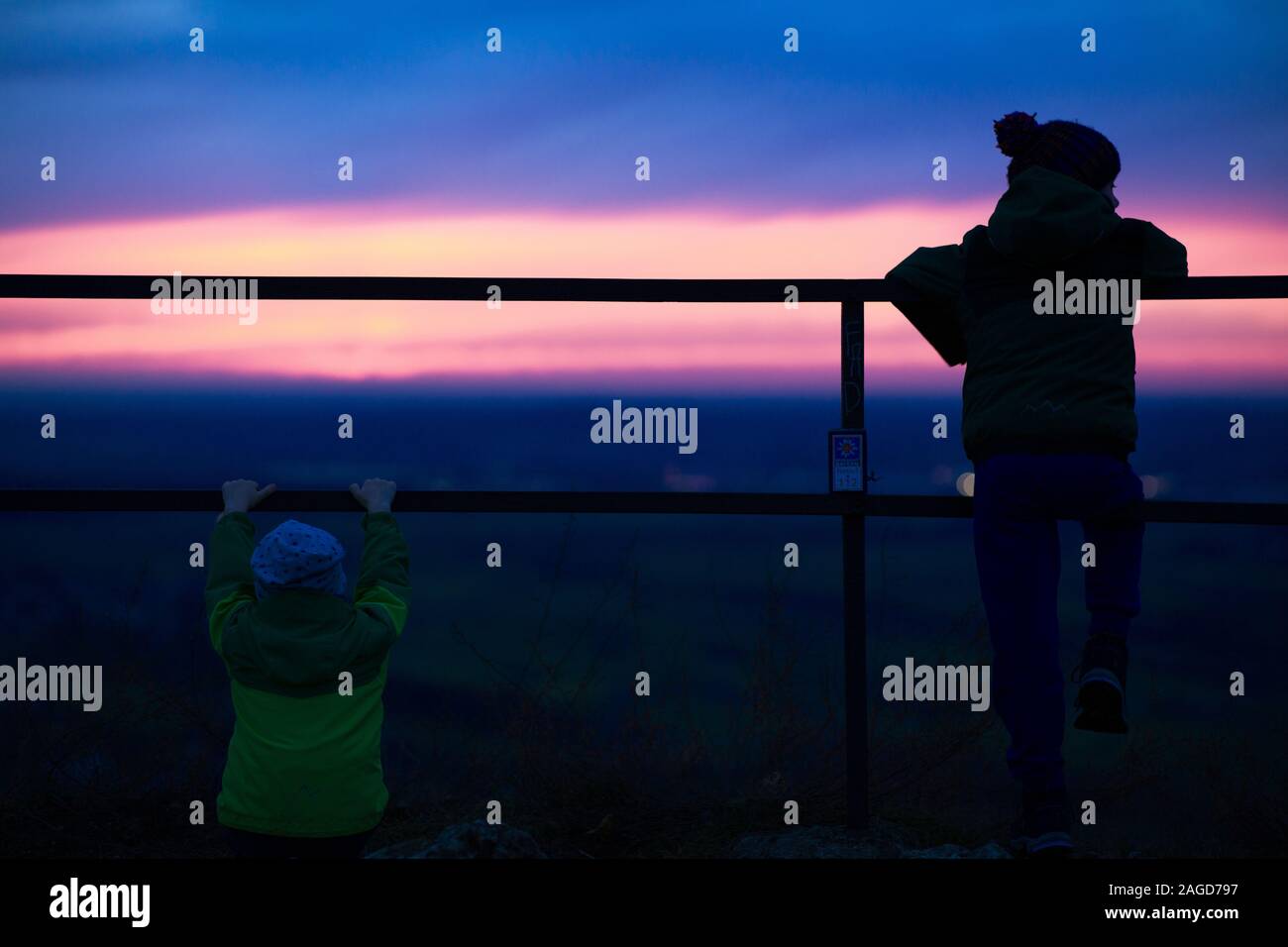 Picture of two kids watching the beautiful sunset near the fences ...