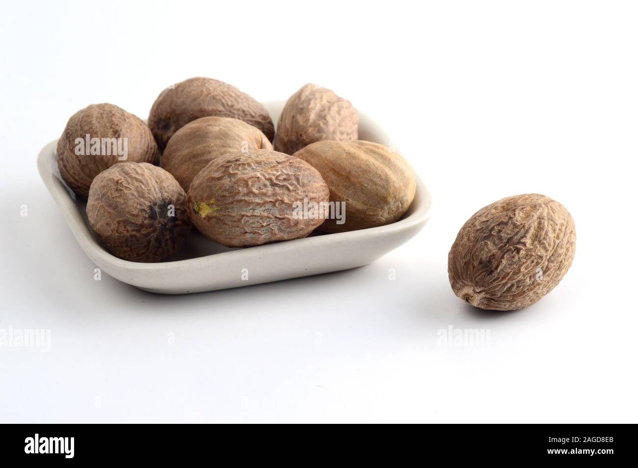 Nutmeg in white plate isolated on white background Stock Photo - Alamy