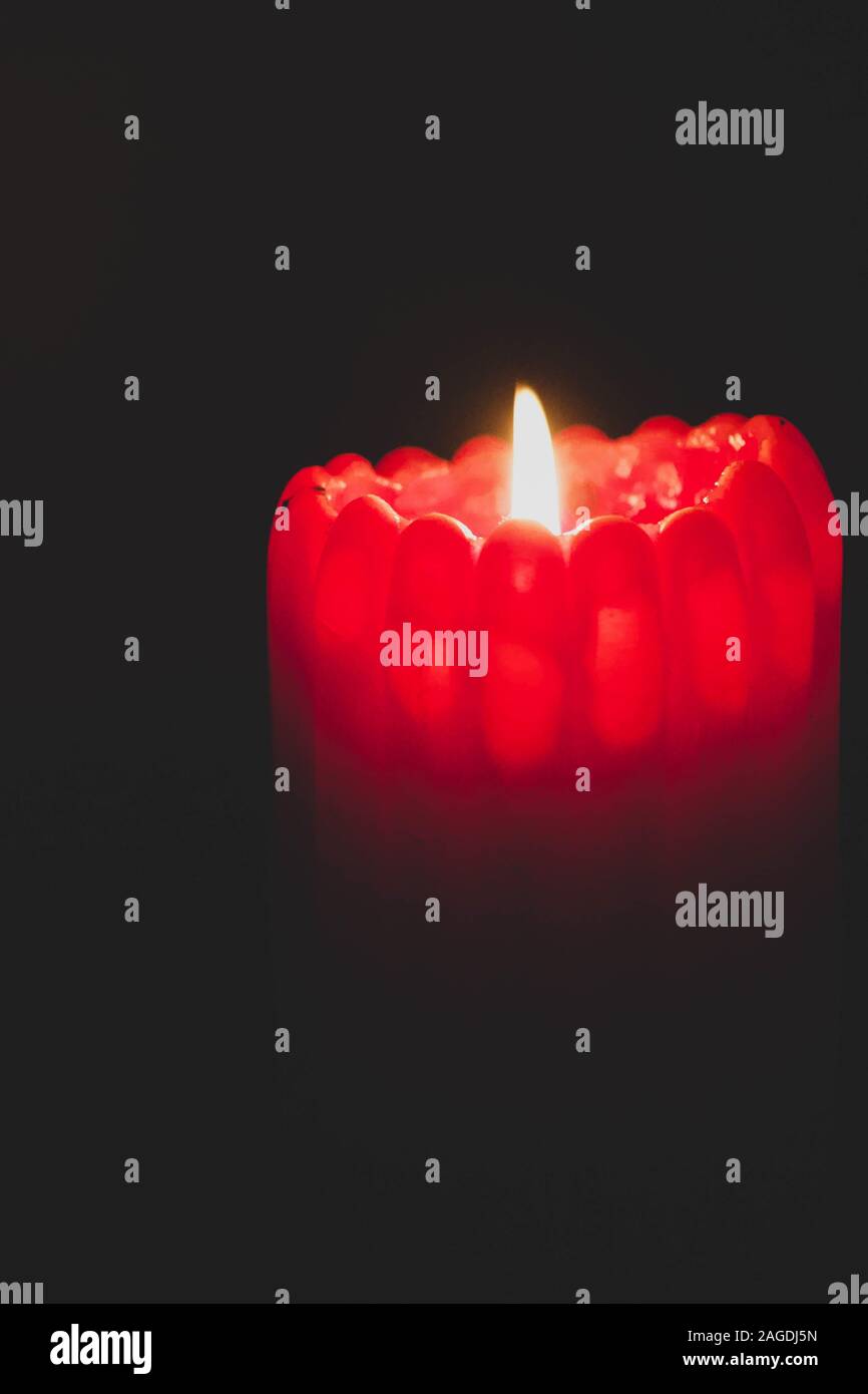 Closeup picture of a lighted red candle with curves on a black ...