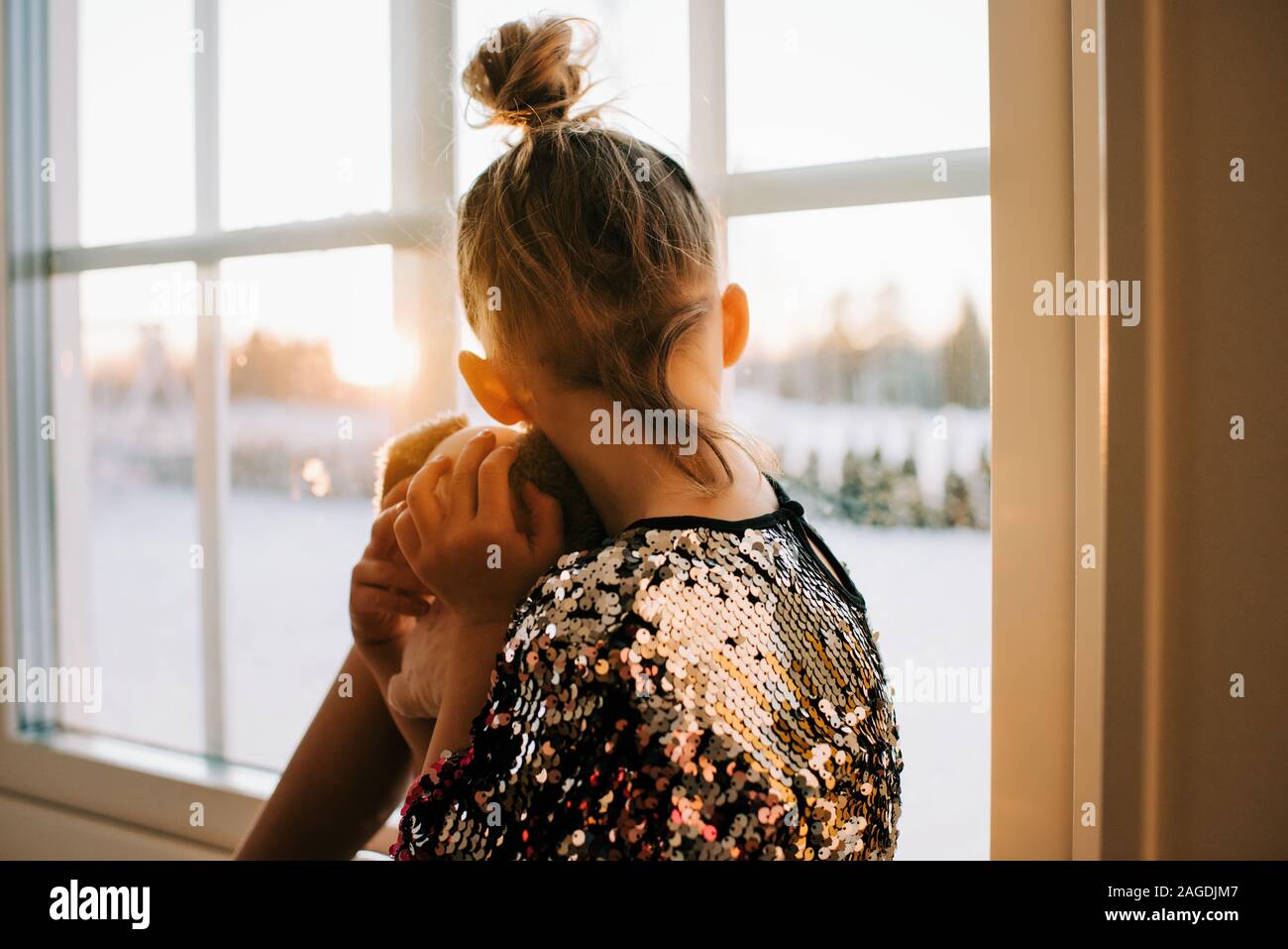 girl looking out a window in a sparkly dress watching the sun go down ...