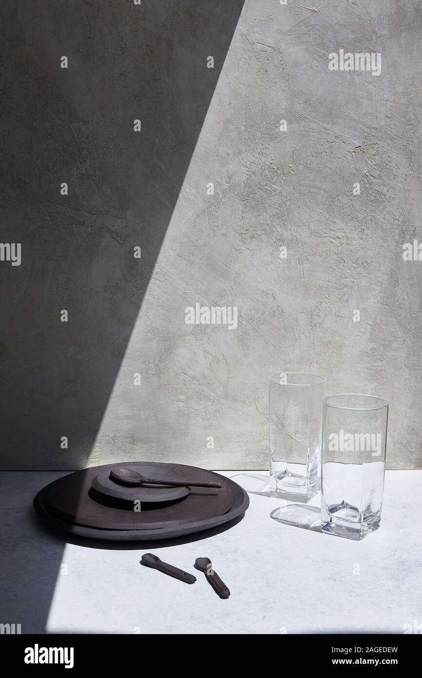 Vertical shot of a black plate and two glass cups on a white table with ...