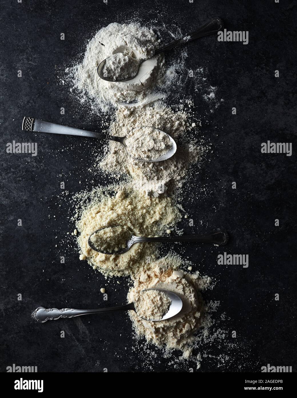 Vertical shot of four spoons in a white flour on a black background ...