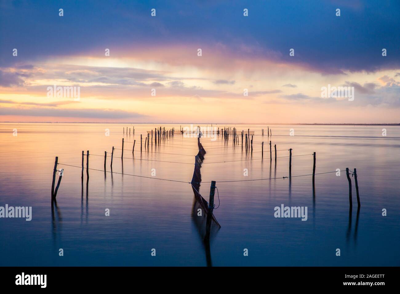 Wooden docks in the ocean with the reflection of light of the sunset in ...