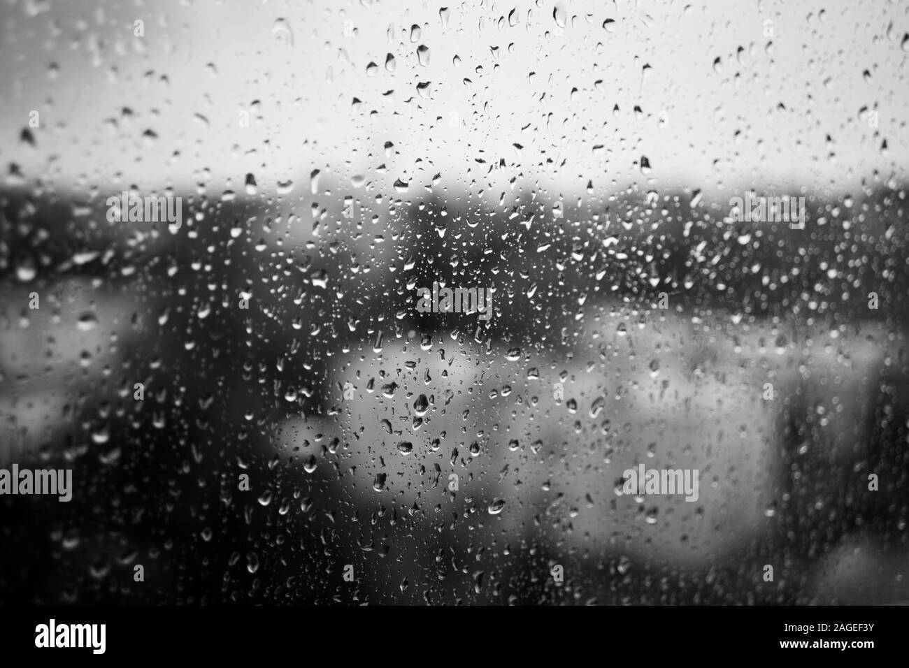 Greyscale shot of glass covered with raindrops on a blurred background ...