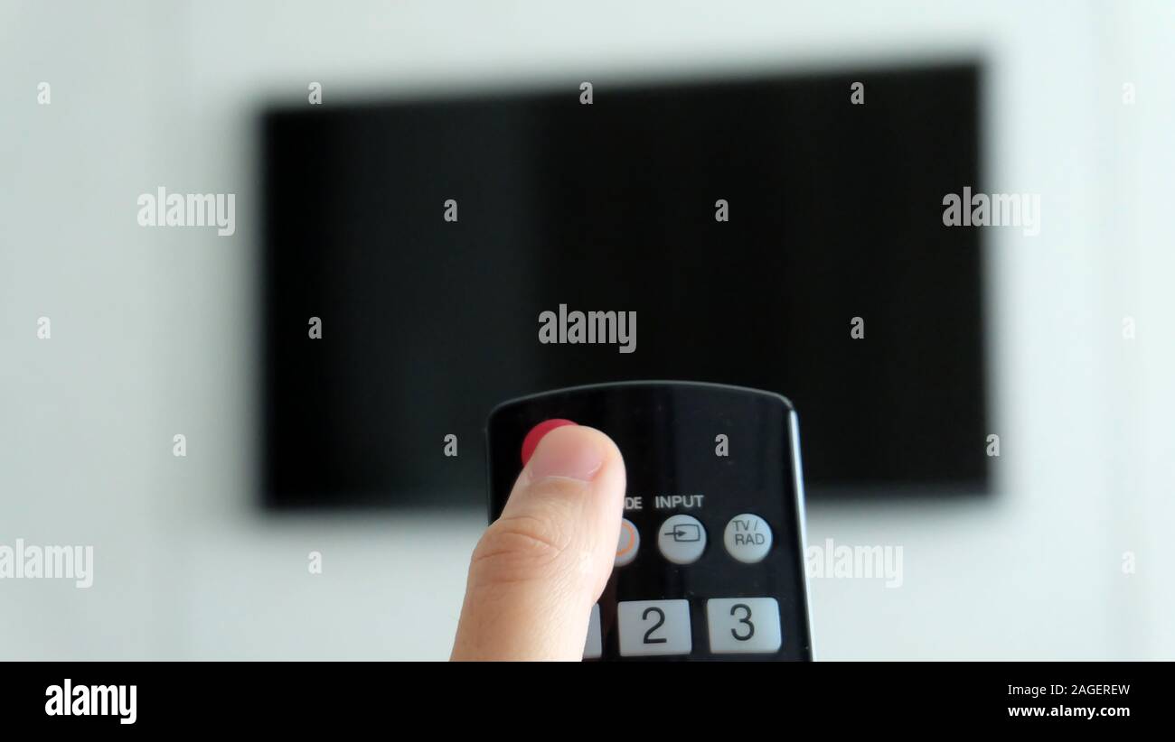 Thumb pressing on the power button of a television remote control ...