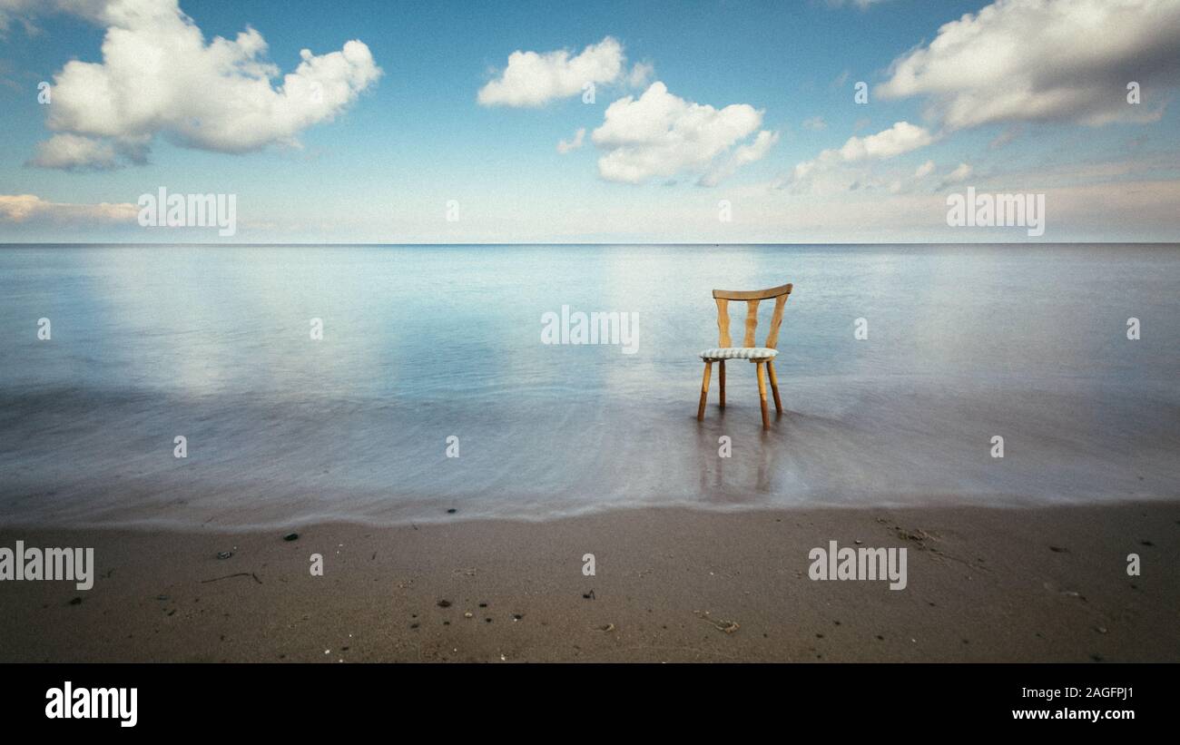 Wooden chair standing at the ocean shore under the sunlight reflecting ...