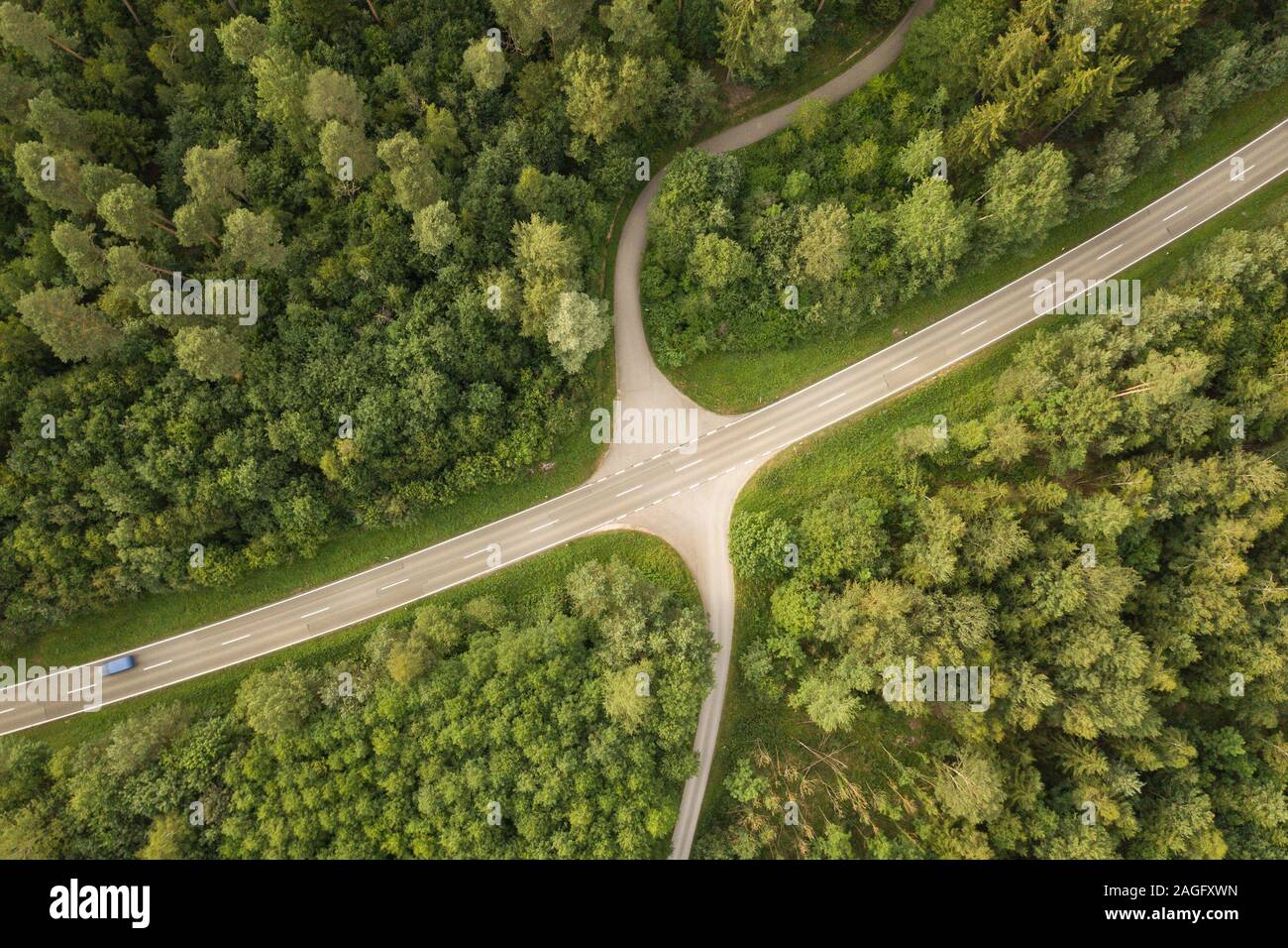 Road with blue car driving and intersection through forest from above ...