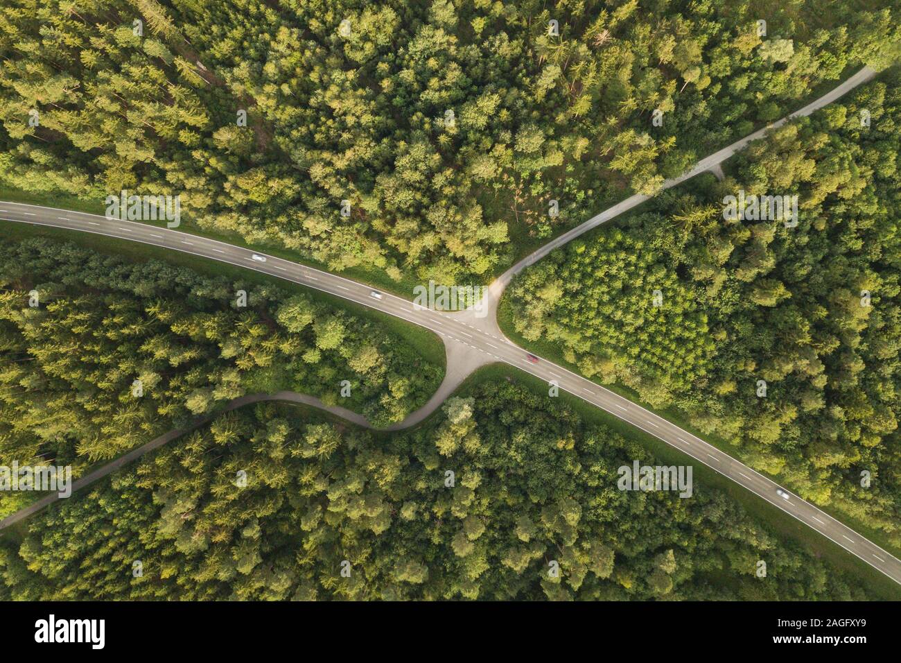 Aerial view of cars driving on road with intersection through forest ...