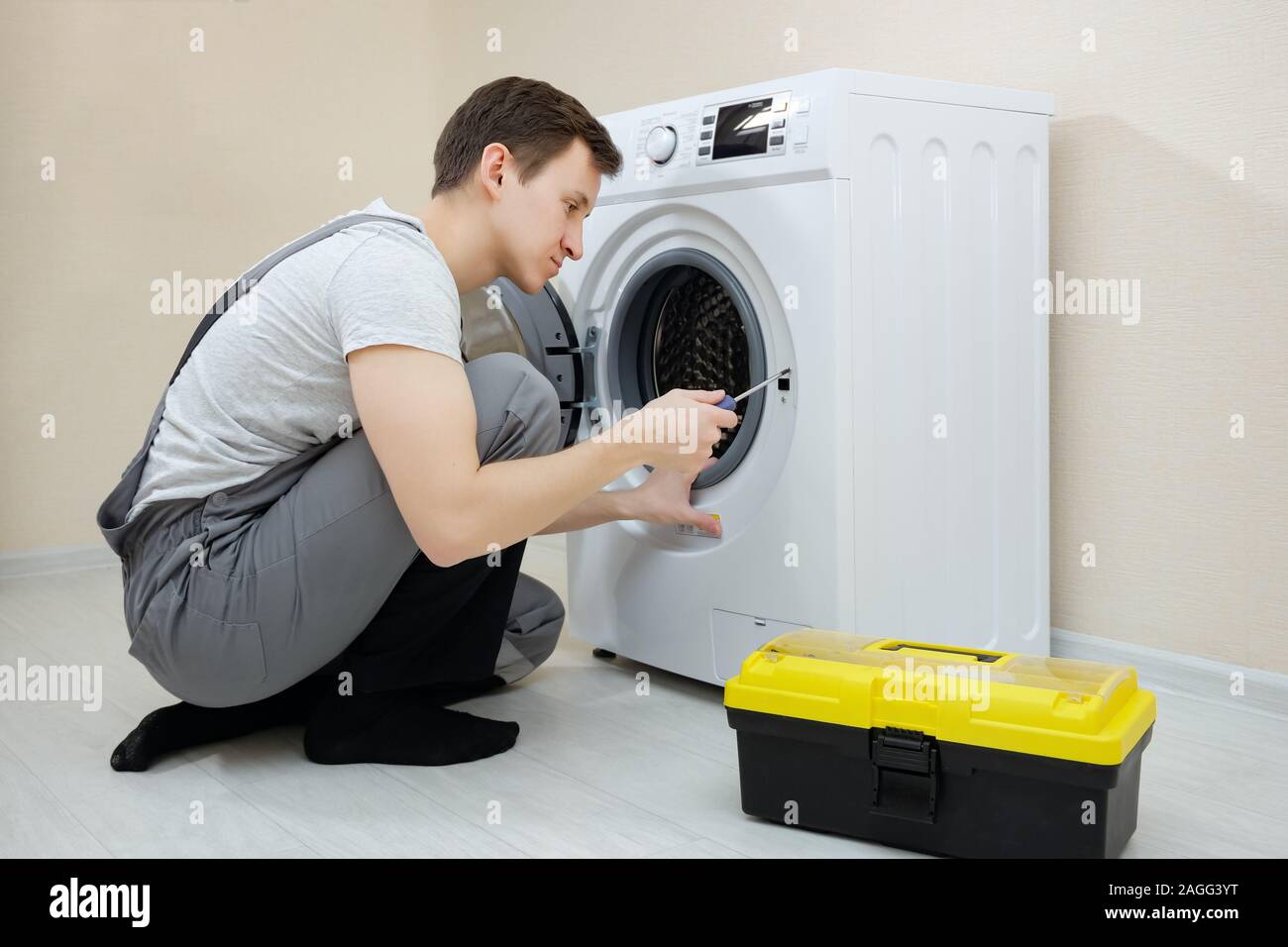 concentrated young man squats repairing broken modern washing machine ...