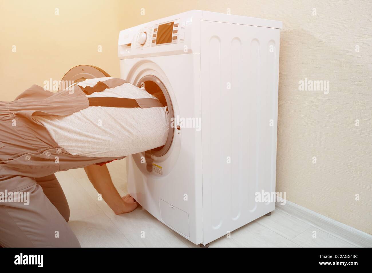 skilled employee in grey uniform gets into repairing broken washing ...