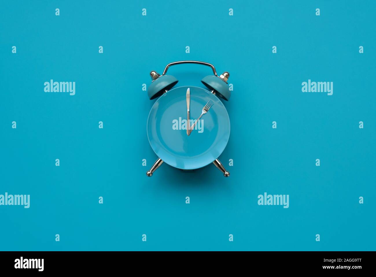 Time to eat. Plate with cutlery as clock on blue background. Top view ...