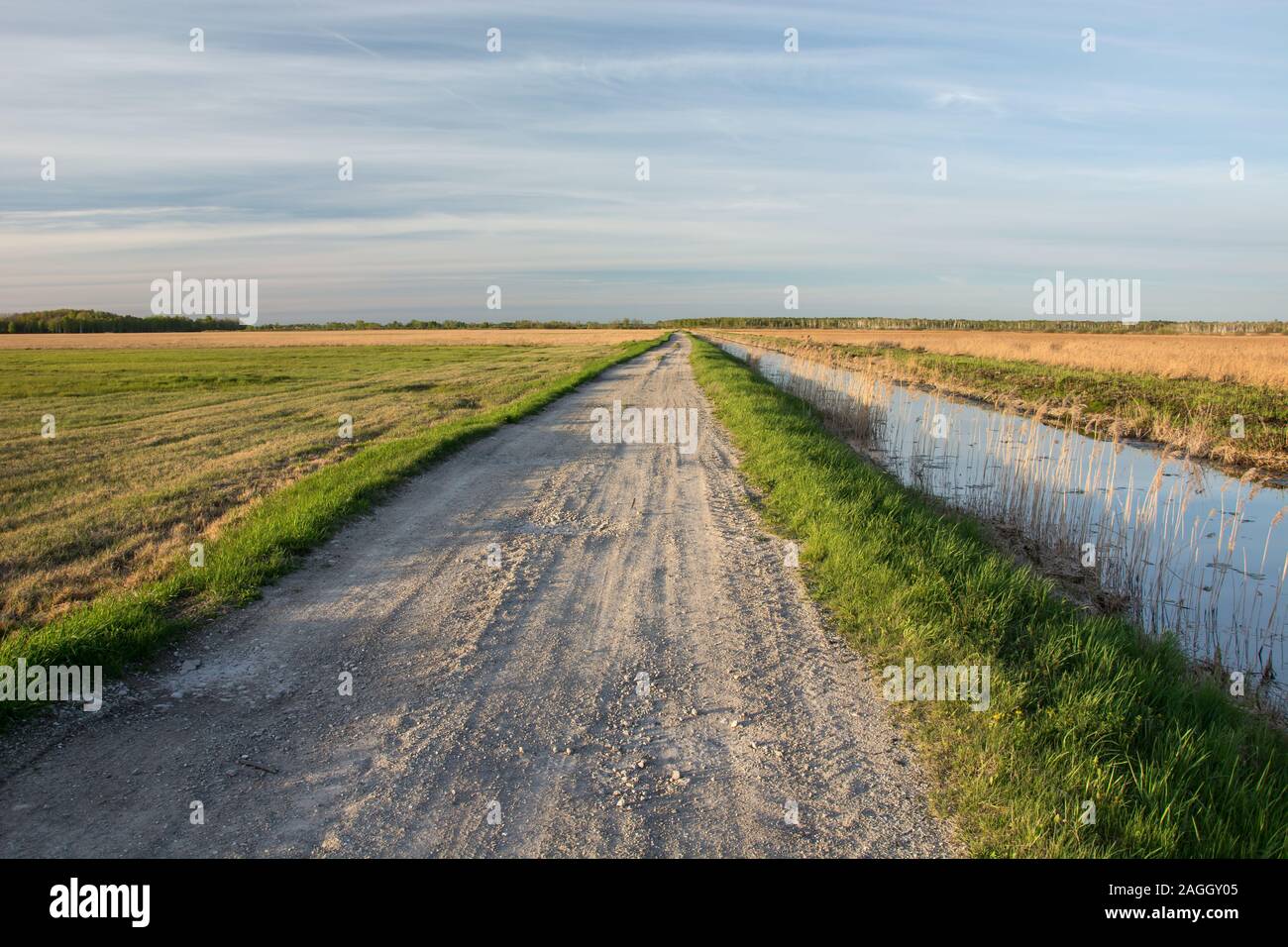 Straight gravel road through a meadow and water channel - view ...