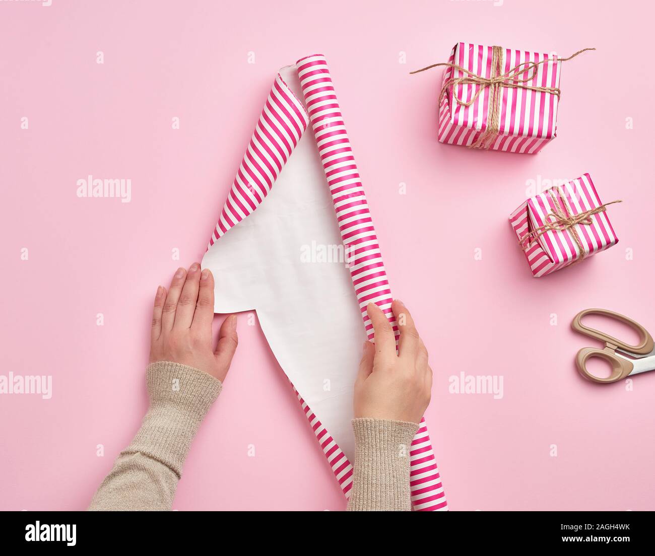 two female hands unfold a roll of wrapping paper, next to two gifts ...
