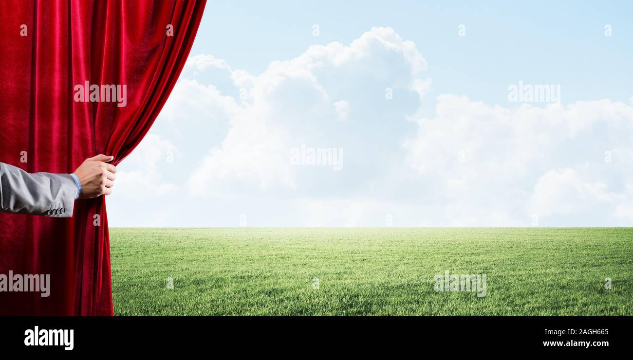 Green meadow behind red curtain and hand holding it Stock Photo - Alamy
