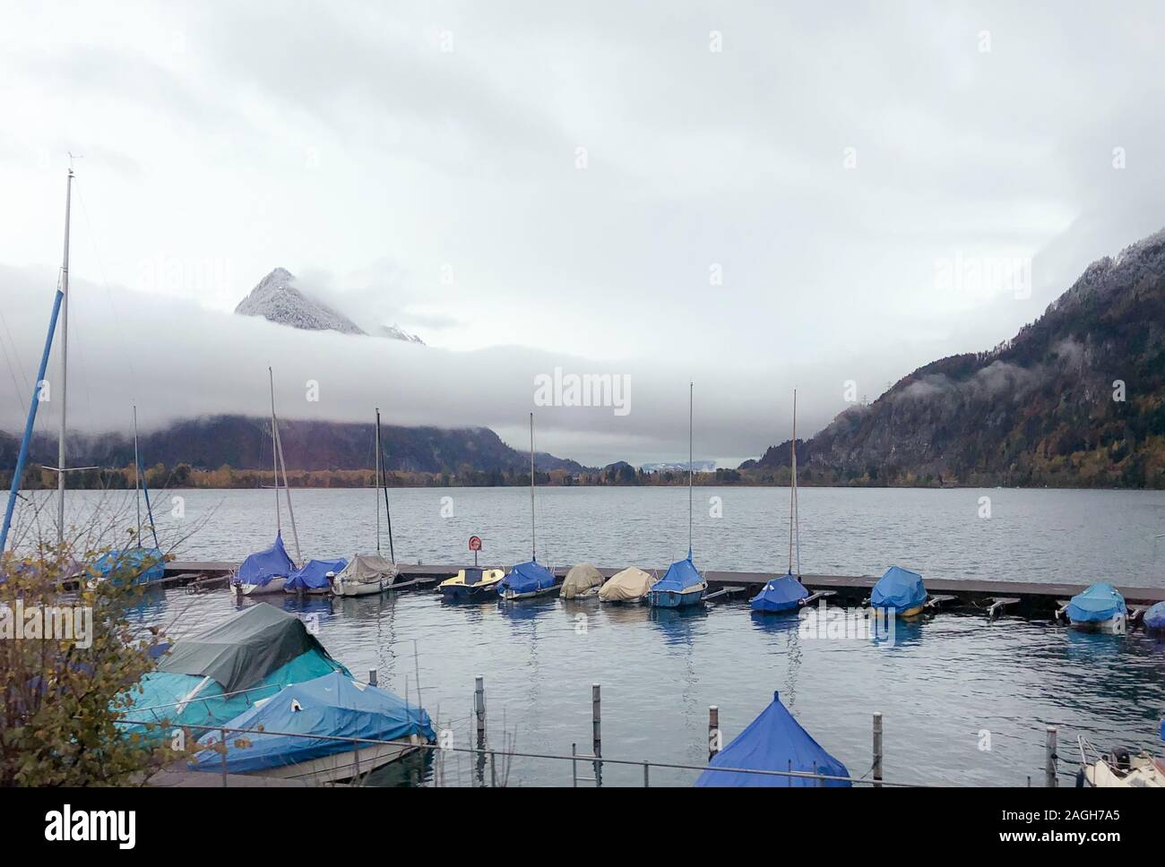 Lake Thun with blue boats on it surrounded by rocks and forests covered ...