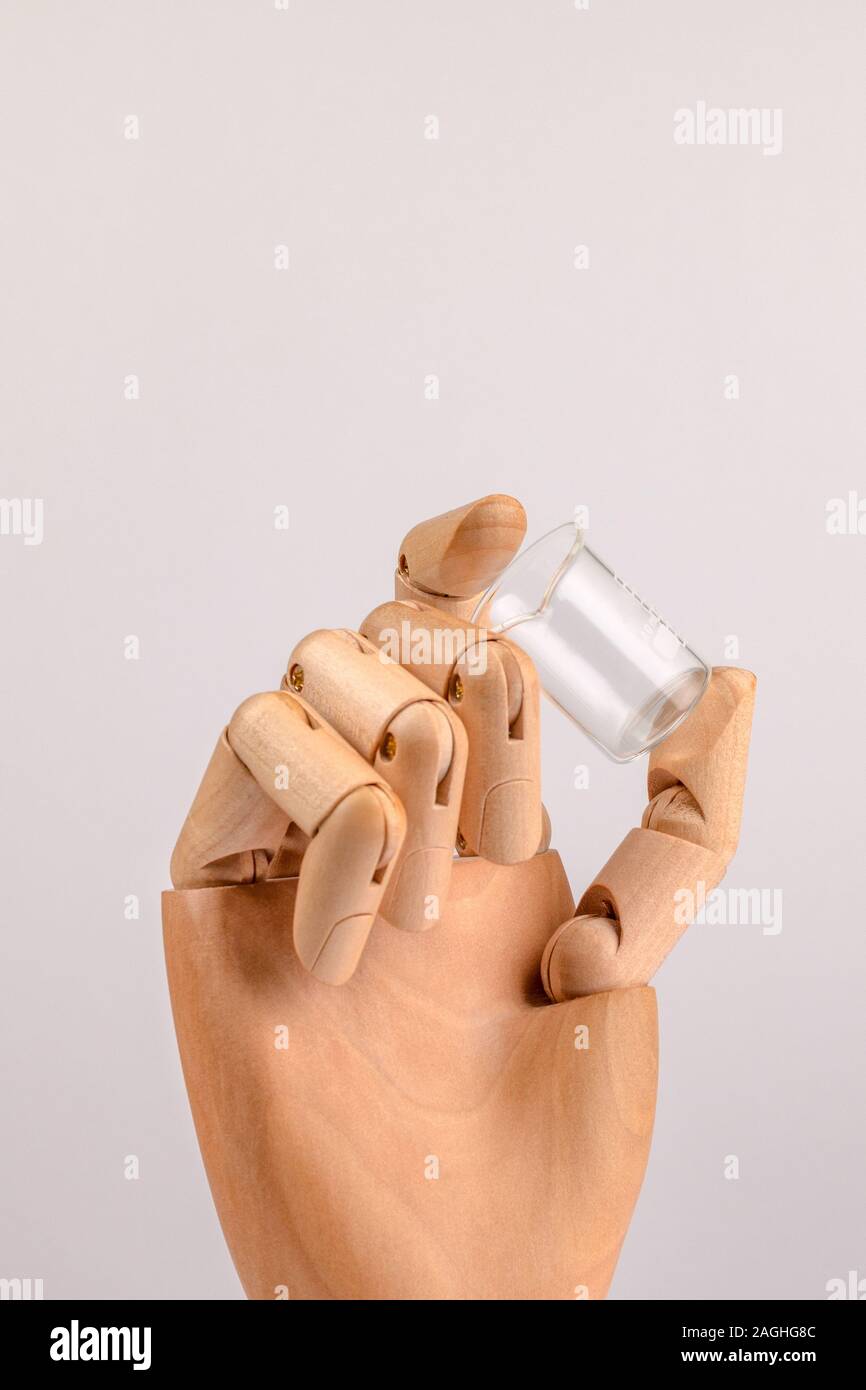 a right wooden hand showing a beaker on a grey background, concept of ...