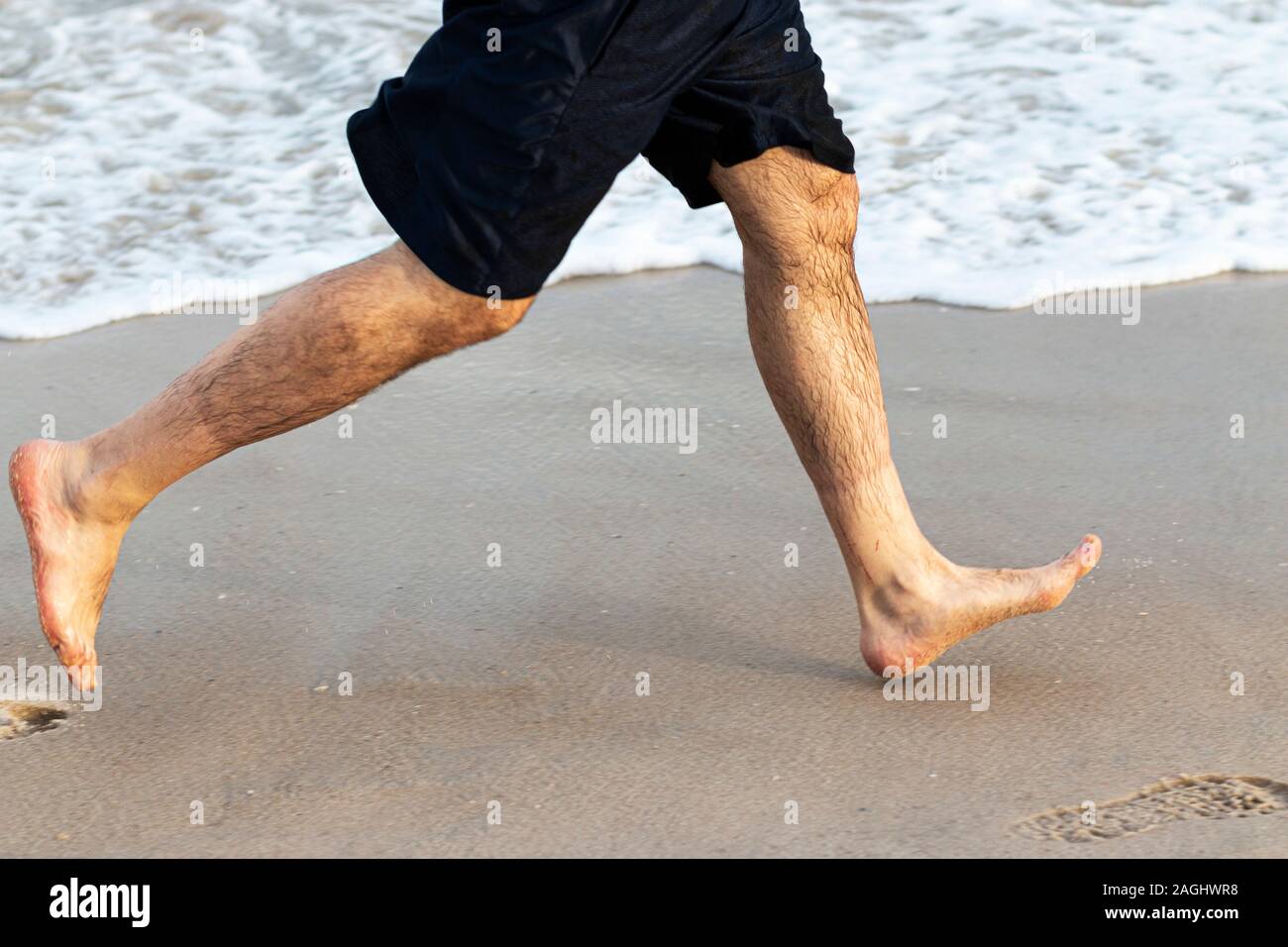 Side view of a runners legs with no shoes on running on the sand of a ...