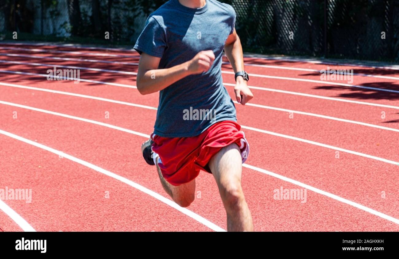 A high school boy is running fast toward the camera on a red track in ...