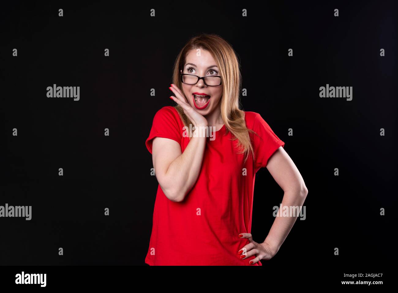 Surprised young woman shouting over black background. Looking at camera ...