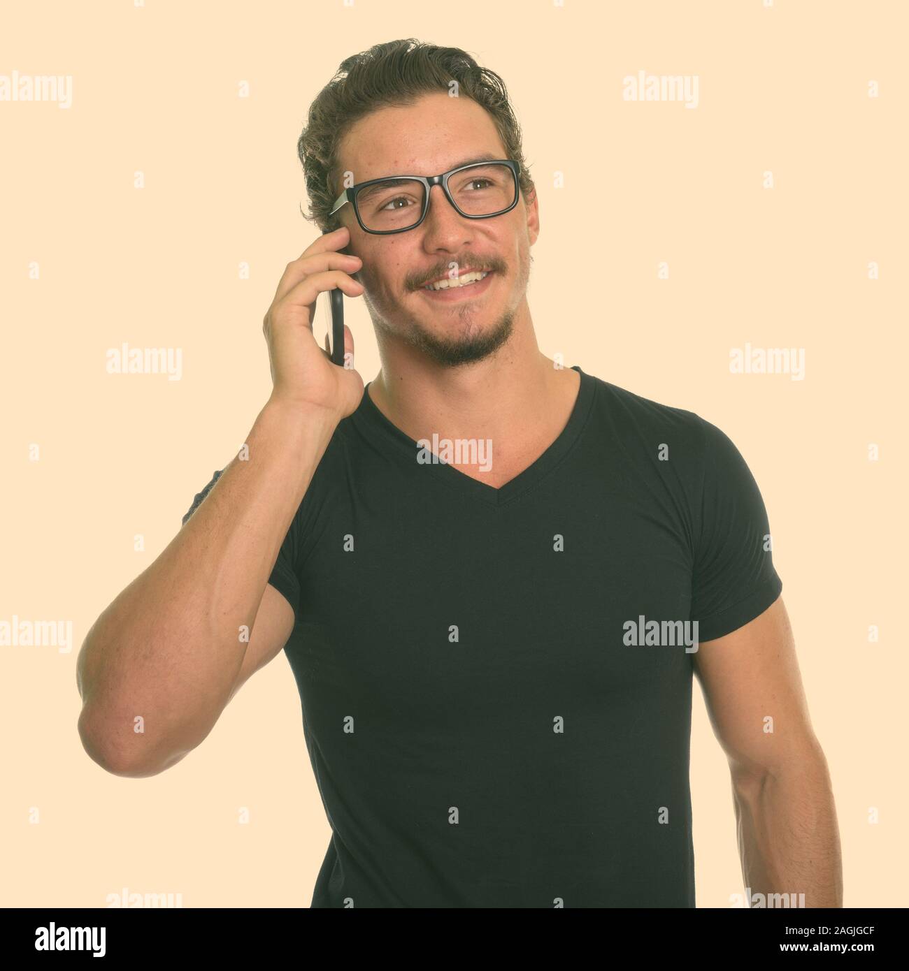 Studio shot of young happy man smiling while talking on mobile phone ...