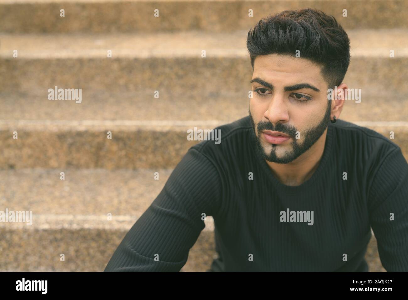 Close up of young handsome Indian man thinking while sitting on the ... Close up of young handsome Indian man thinking while sitting on the ...