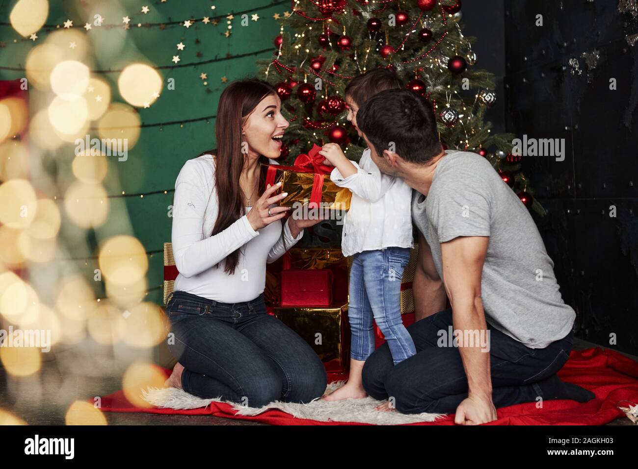Surprised look. Lovely family sits near the Christmas tree with gift ...