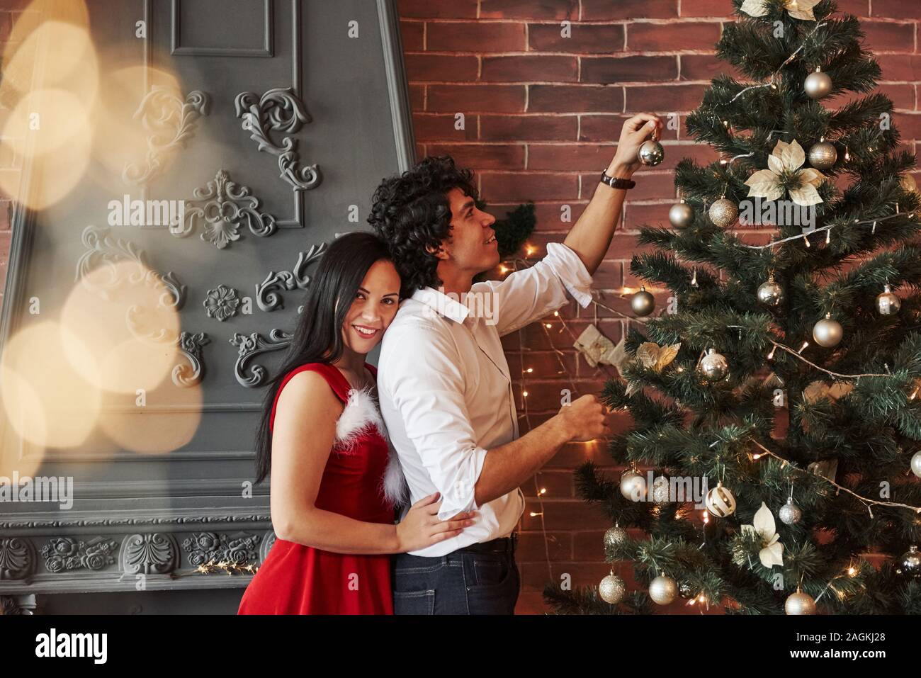 Romantic couple dressing up Christmas tree in the room with brown wall ...
