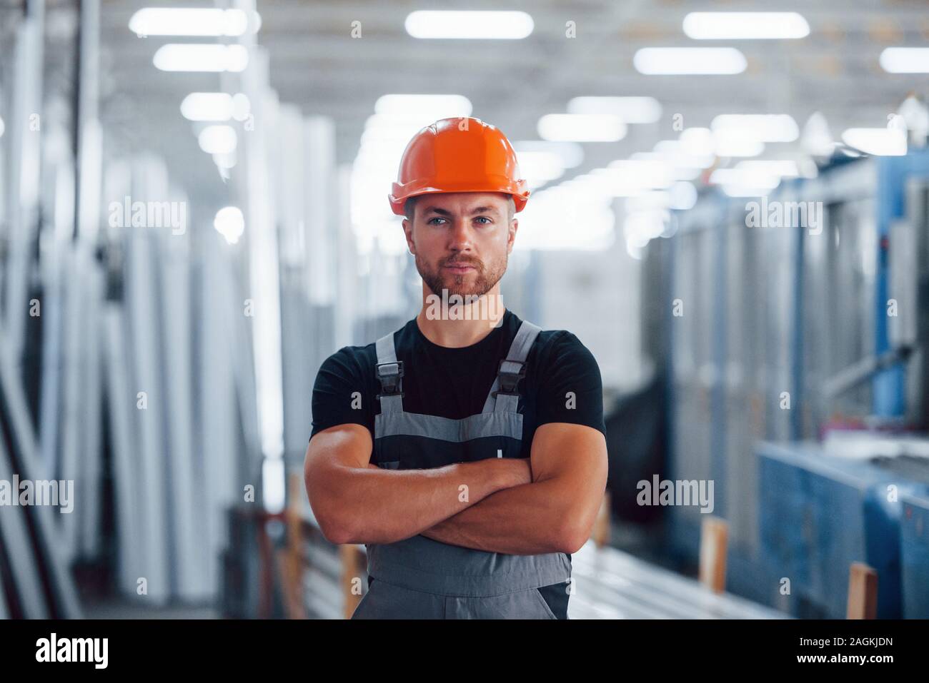 Stands with arms crossed. Portrait of male industrial worker indoors in ...