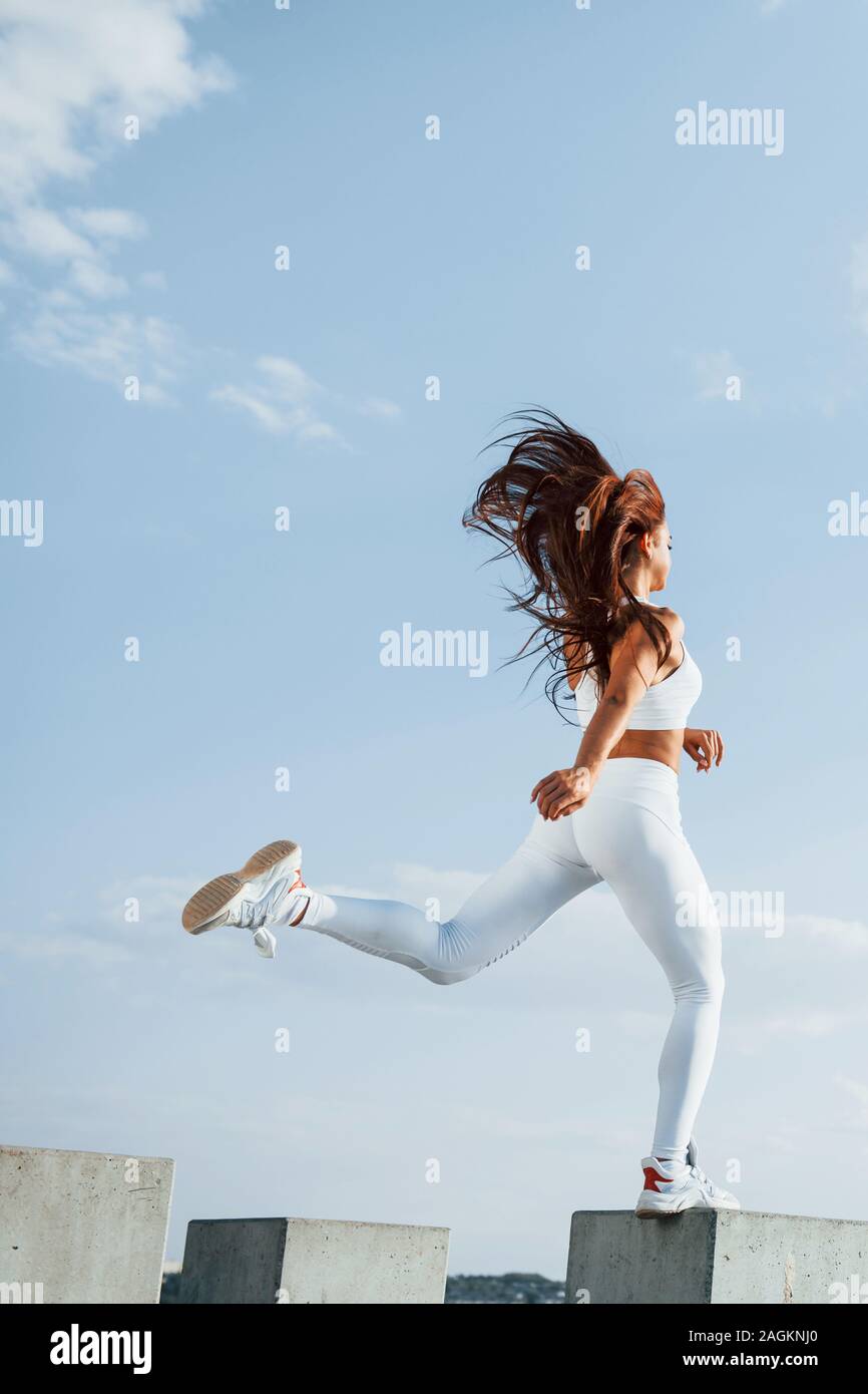 Up in the sky. Female runner in white sportive clothes doing fitness ...