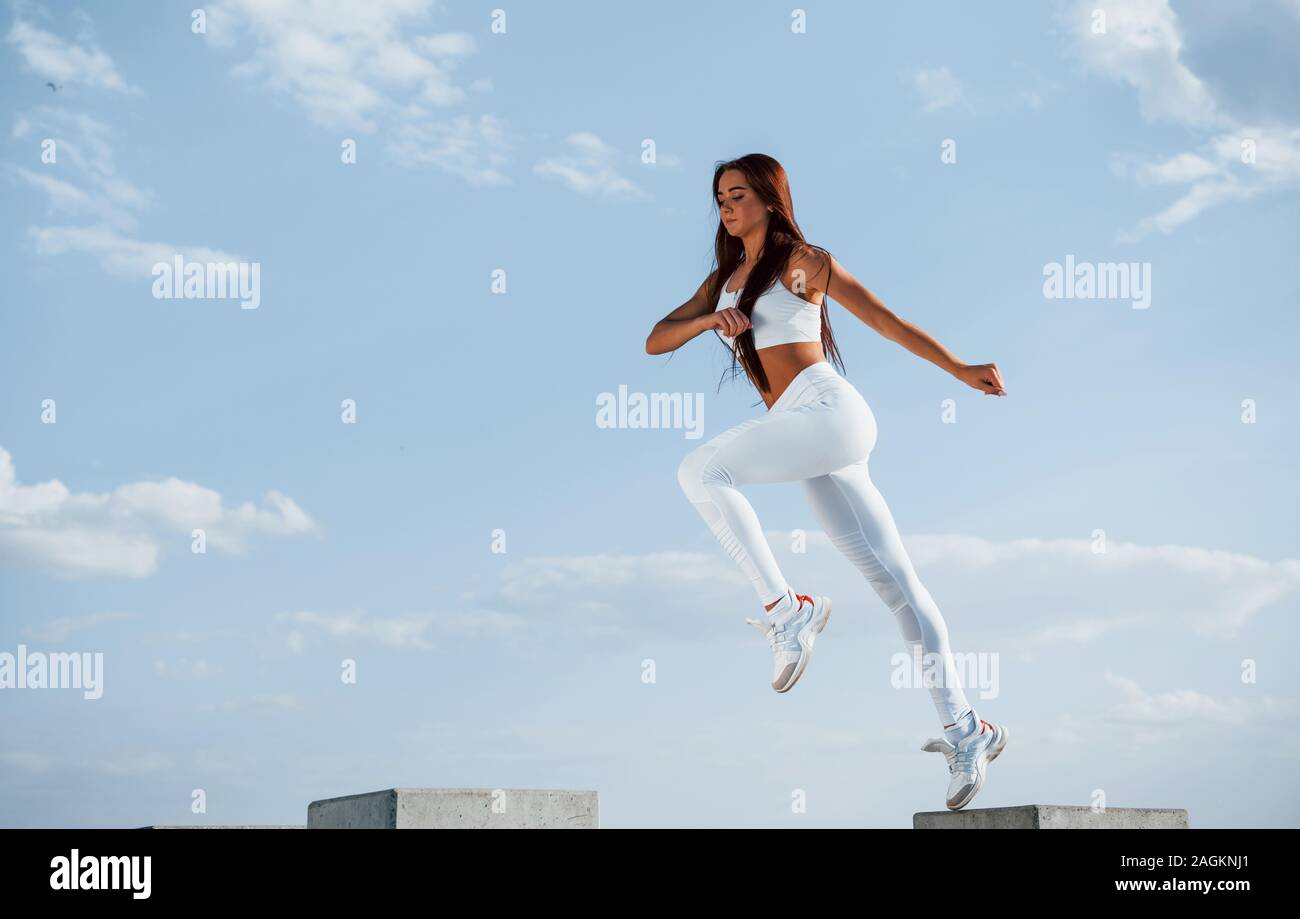 Up in the sky. Female runner in white sportive clothes doing fitness ...