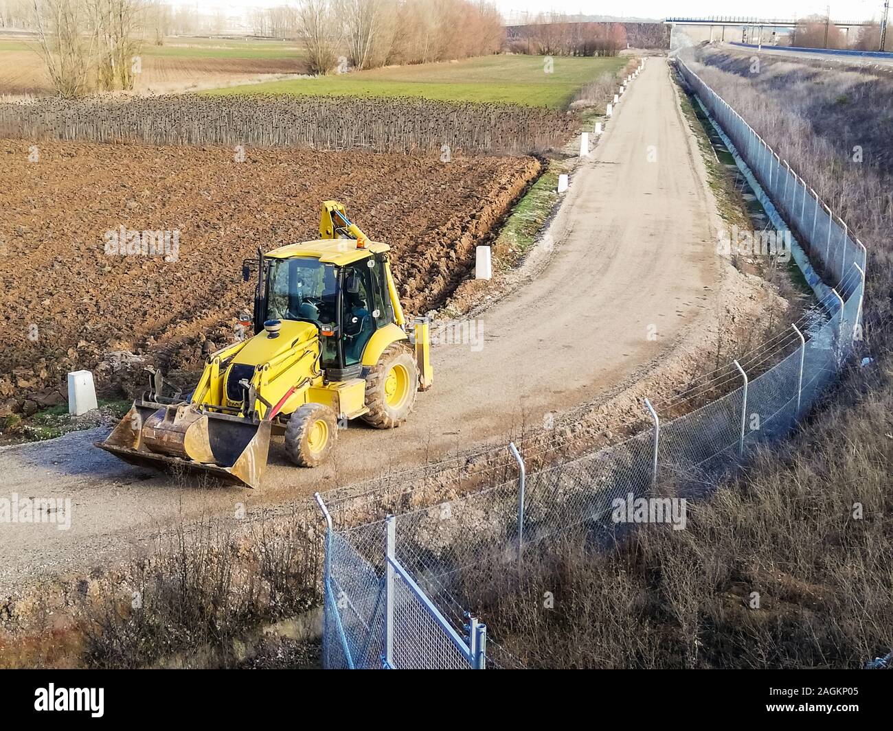 A backhoe loader circulating on a dirt road between crops next to a ...