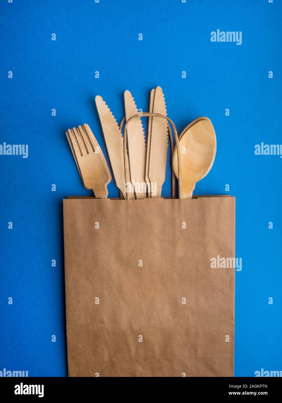 Disposable wooden cutlery in paper bag on trendy blue color background ...