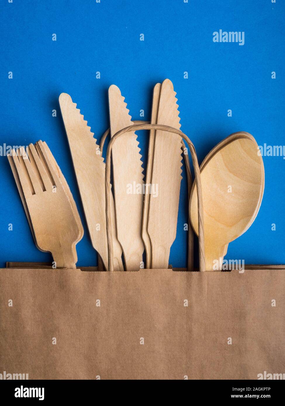 Disposable wooden cutlery in paper bag on trendy blue color background ...