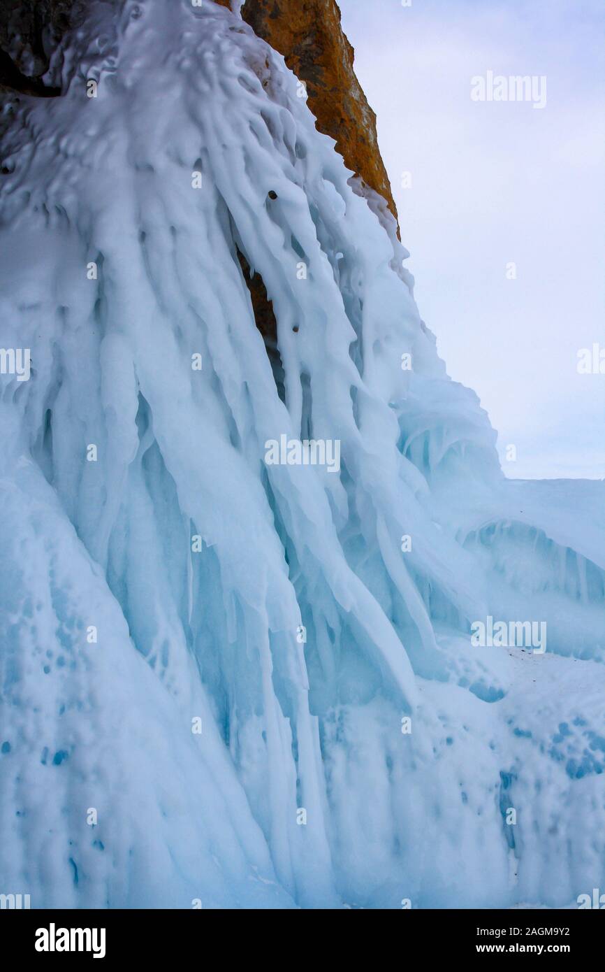 Long curved icicles melted in the sun hang on a rock. Smooth ice ...