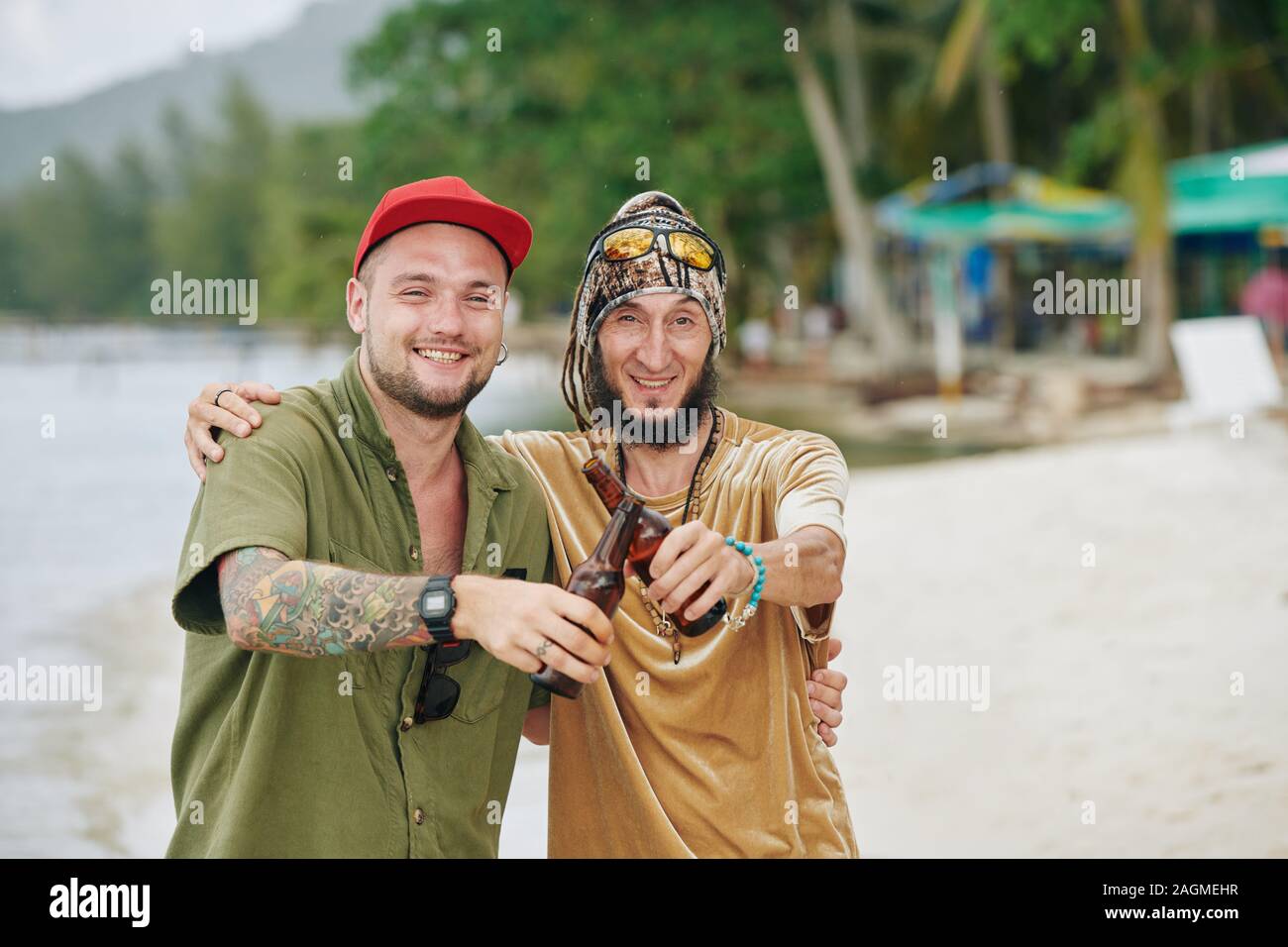Happy smiling friends hugging and clinking bottles of cold beer when ...