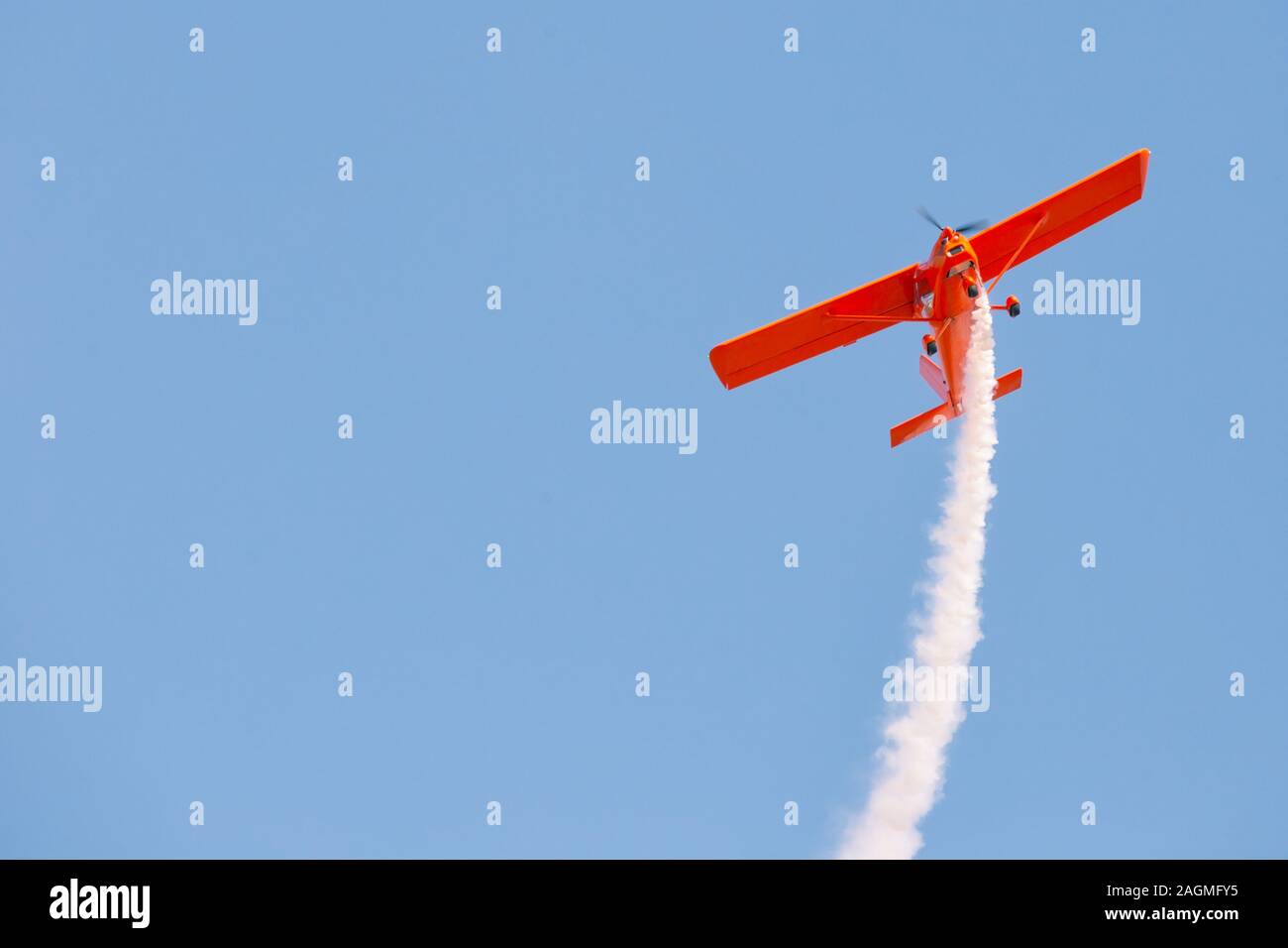 Red glider plane emits white smoke in a blue sky. Air show Stock Photo ...
